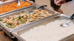 Buffet com diversas opções de comida, incluindo arroz, um prato de frango e um refogado de legumes.