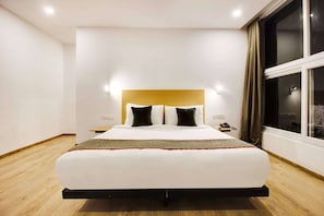 Quarto de hotel moderno com cama grande, cabeceira de madeira, mesa de cabeceira com telefone e janela com cortinas.
