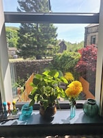 Janela com vista para um jardim, uma parede de pedra e um edifício ao fundo.