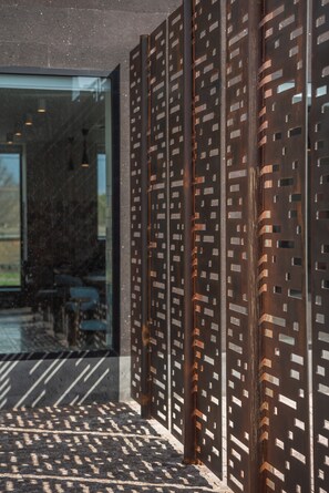 Entrada de um edifício moderno com piso padronizado e divisória metálica com cortes geométricos.