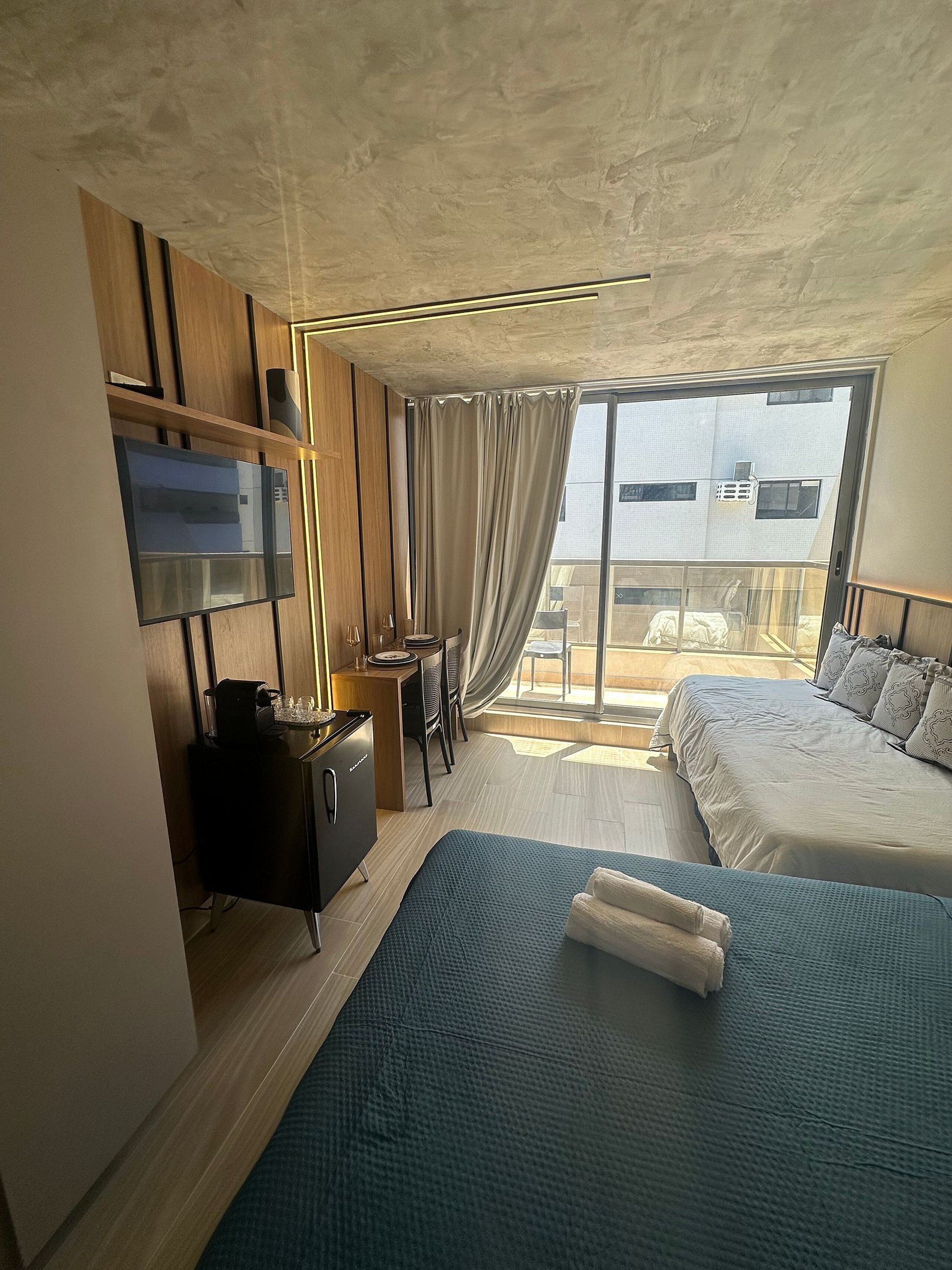 Quarto de hotel com cama, escrivaninha, televisão e vista da cidade.