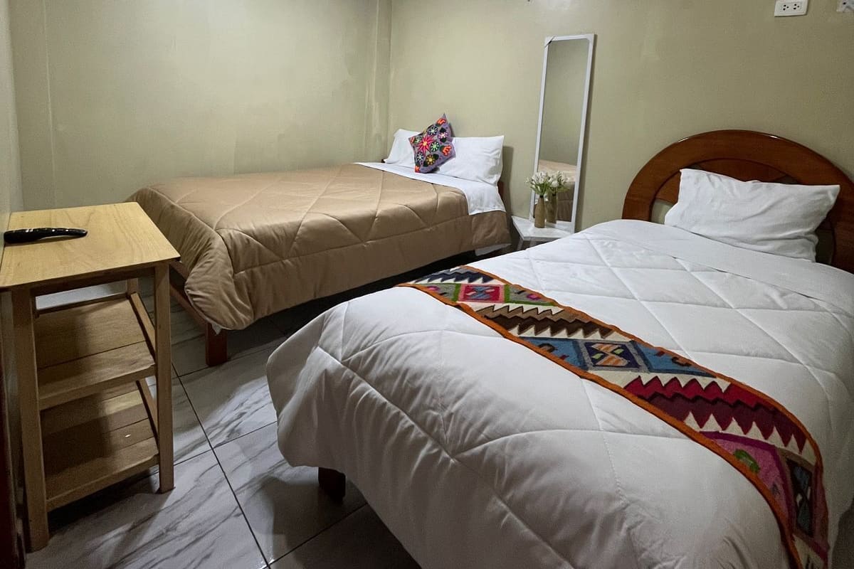 Quarto de hotel com duas camas, uma escrivaninha e um espelho.
