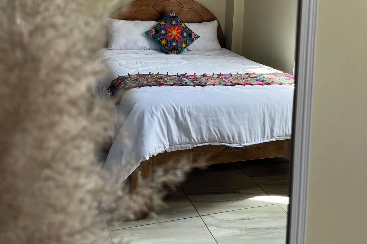 Um quarto com uma cama, um travesseiro colorido e um cobreleito branco.