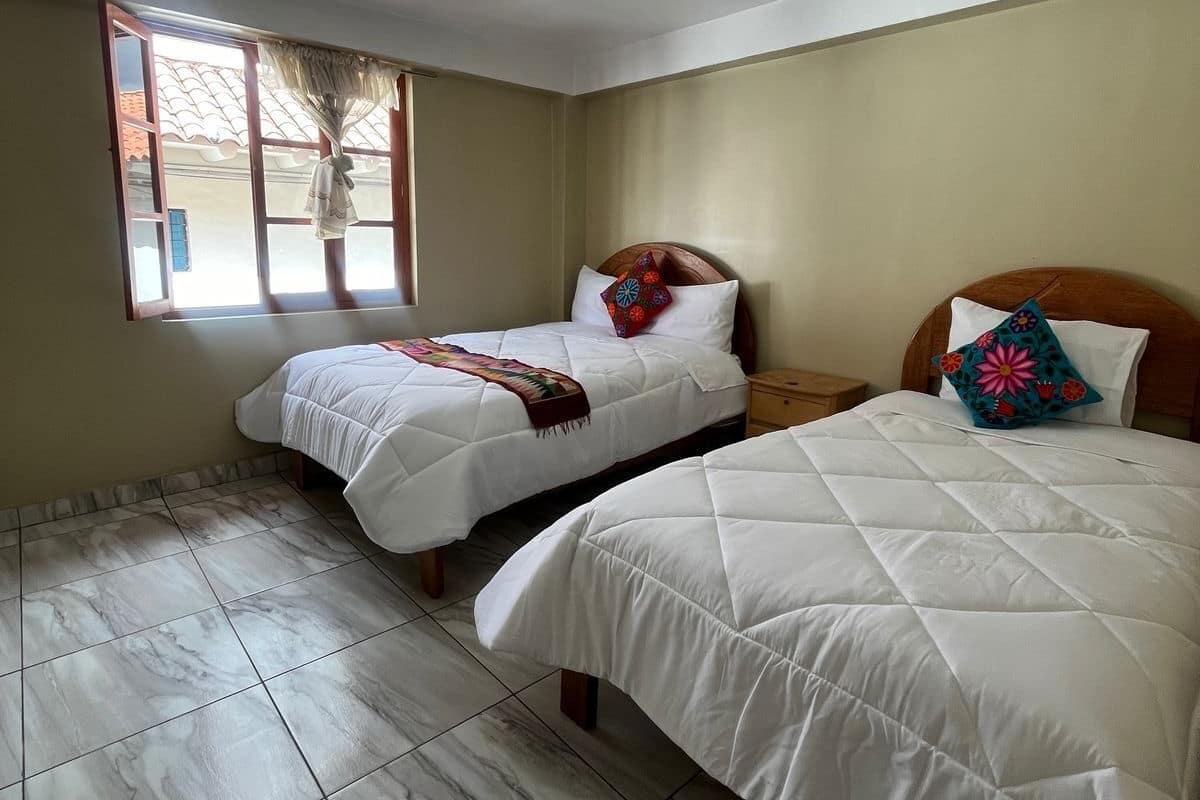 Quarto com duas camas, ventilador de teto e janela com cortinas.