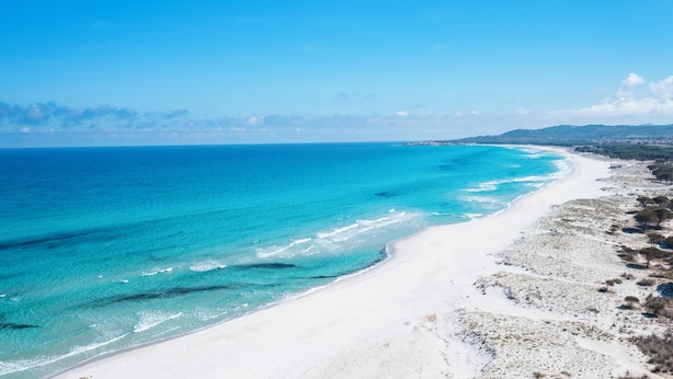 Paisagem costeira com uma praia de areia e águas azul-claras.