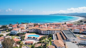 Um resort costeiro com piscina, vários edifícios e uma praia ao fundo.