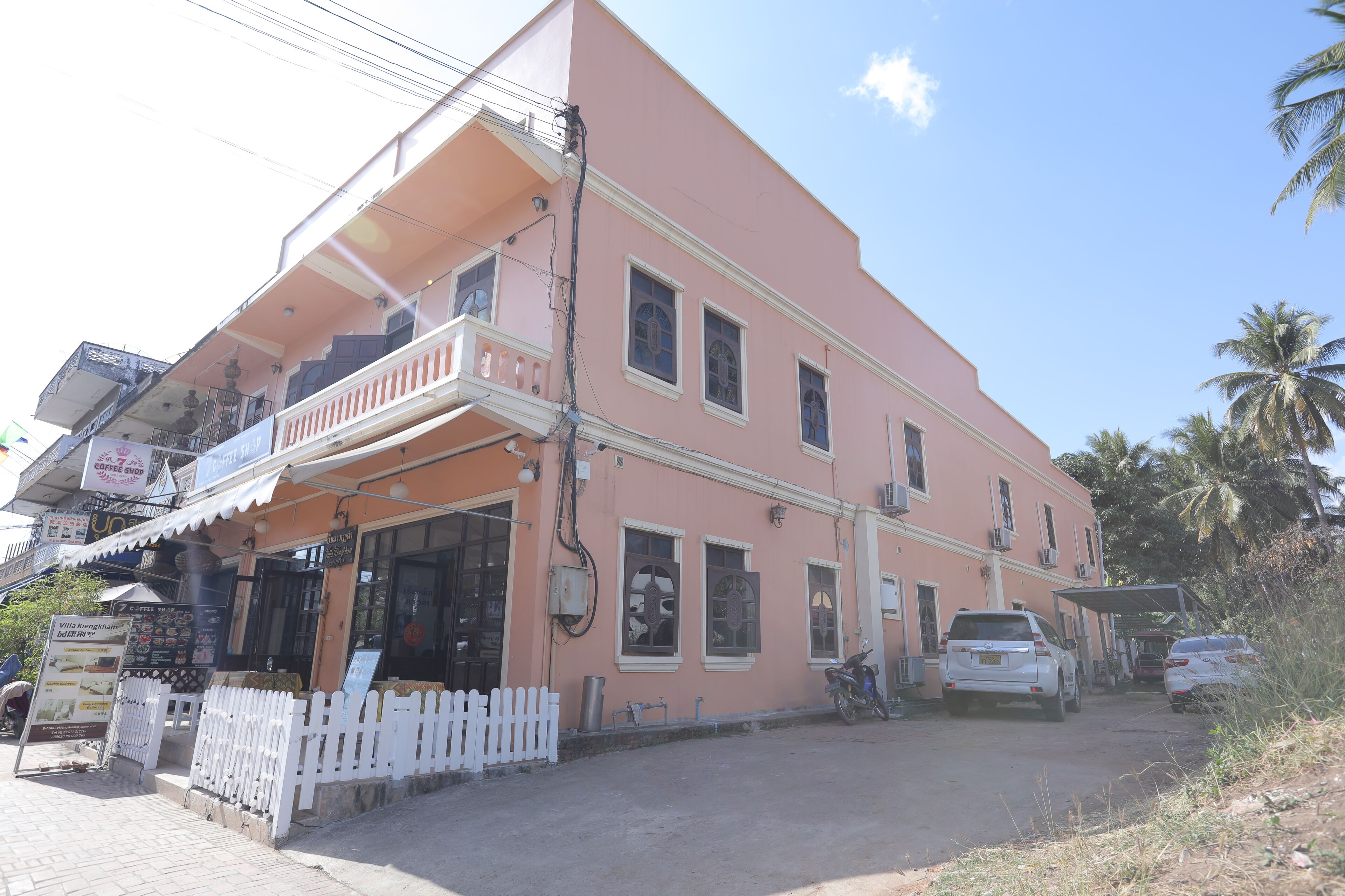 Um edifício rosa com varanda, cerca branca de piquete e um carro estacionado.