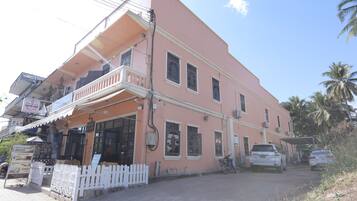 Um edifício rosa com varanda, cerca branca de piquete e um carro estacionado.