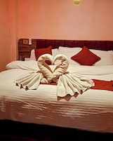 Quarto de hotel com uma cama, toalhas dispostas em formato de coração e almofadas vermelhas.