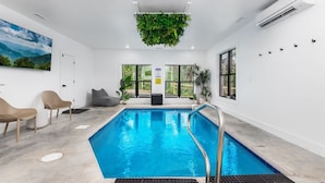 Piscina interior moderna com água azul cristalina, cercada por paredes brancas e grandes janelas.