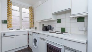 Cozinha compacta com armários brancos, máquina de lavar, forno e cafeteira.