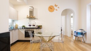 Cozinha moderna com mesa e cadeiras de vidro, relógio na parede e ilha com eletrodomésticos.