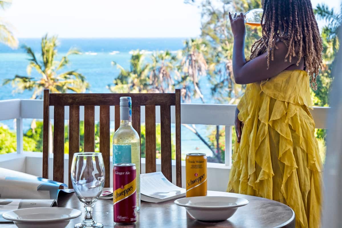 Uma mesa com uma garrafa de vinho, um copo, uma lata de Schweppes e um menu numa varanda com vista para o oceano.