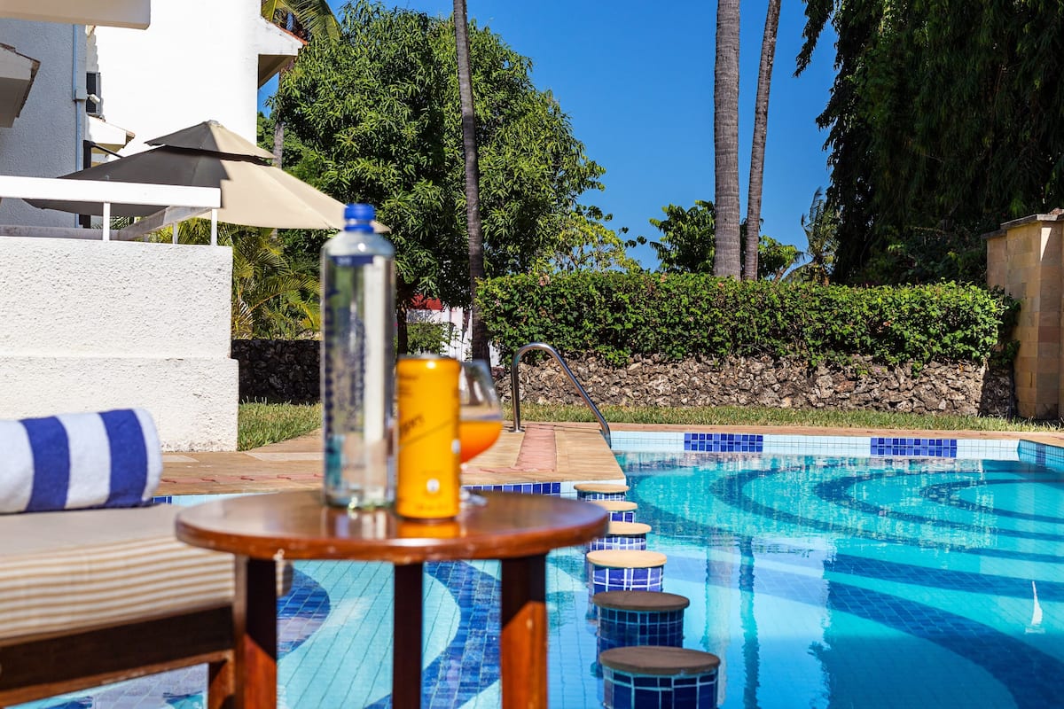 Uma área de piscina com piscina azul límpida, cadeiras de lounge e uma mesa com garrafa e copo.