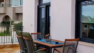 Um pátio externo com mesa e cadeiras, uma pérgula e vista para um edifício com grandes janelas.