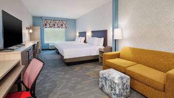 Quarto de hotel com cama, sofá, televisão, escrivaninha e cadeira.