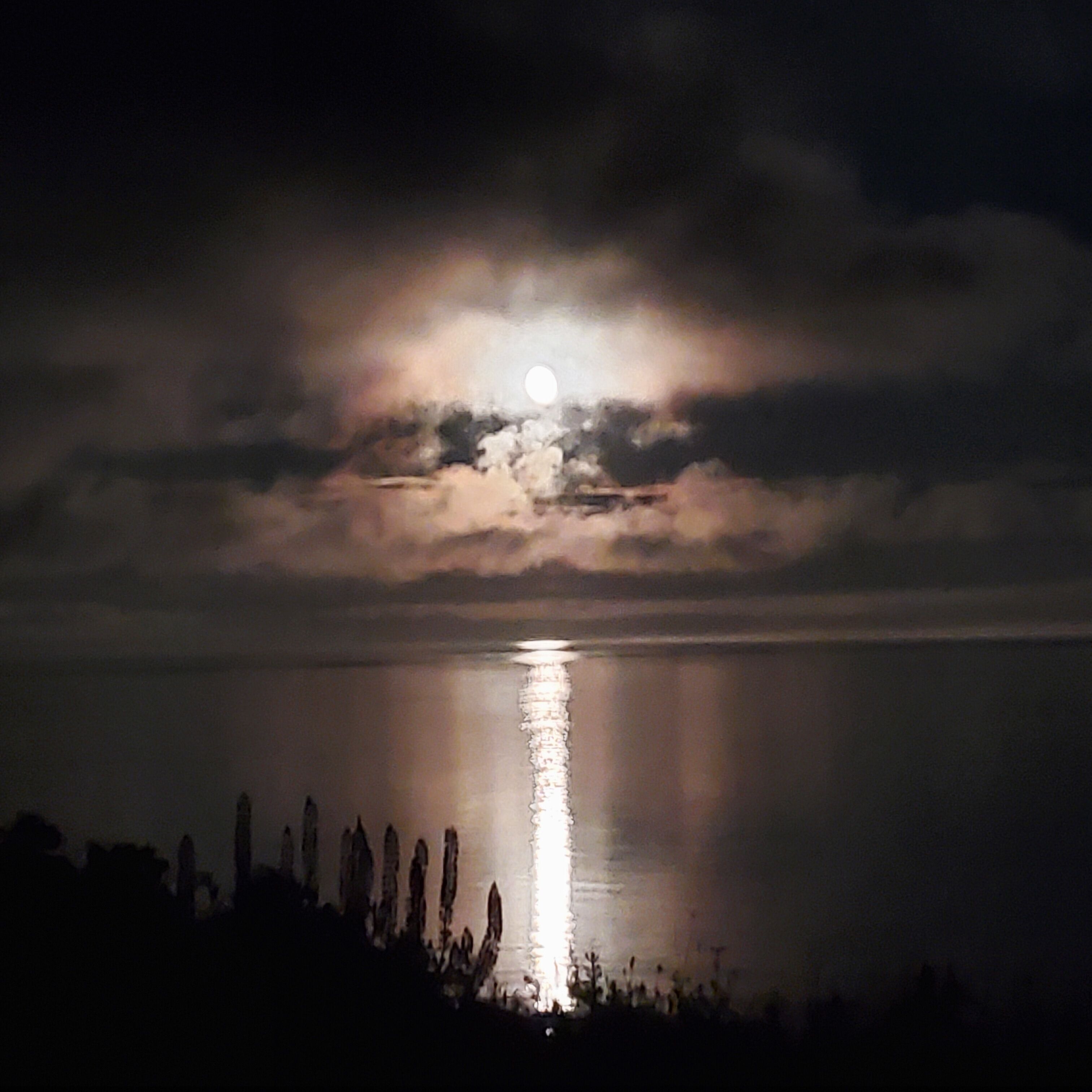 Cena noturna com uma lua cheia refletida em águas calmas, cercada por nuvens.