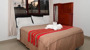 Cama bem arrumada com colcha marrom e manta listrada em vermelho e marrom, travesseiros brancos e uma toalha branca sobre a cama.