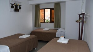 Quarto de hotel com duas camas de solteiro, janela com cortinas, cabideiro e prateleira com amenities de higiene pessoal.