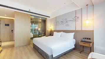 Quarto de hotel moderno com cama grande, mesas de cabeceira, escrivaninha e divisória de vidro.