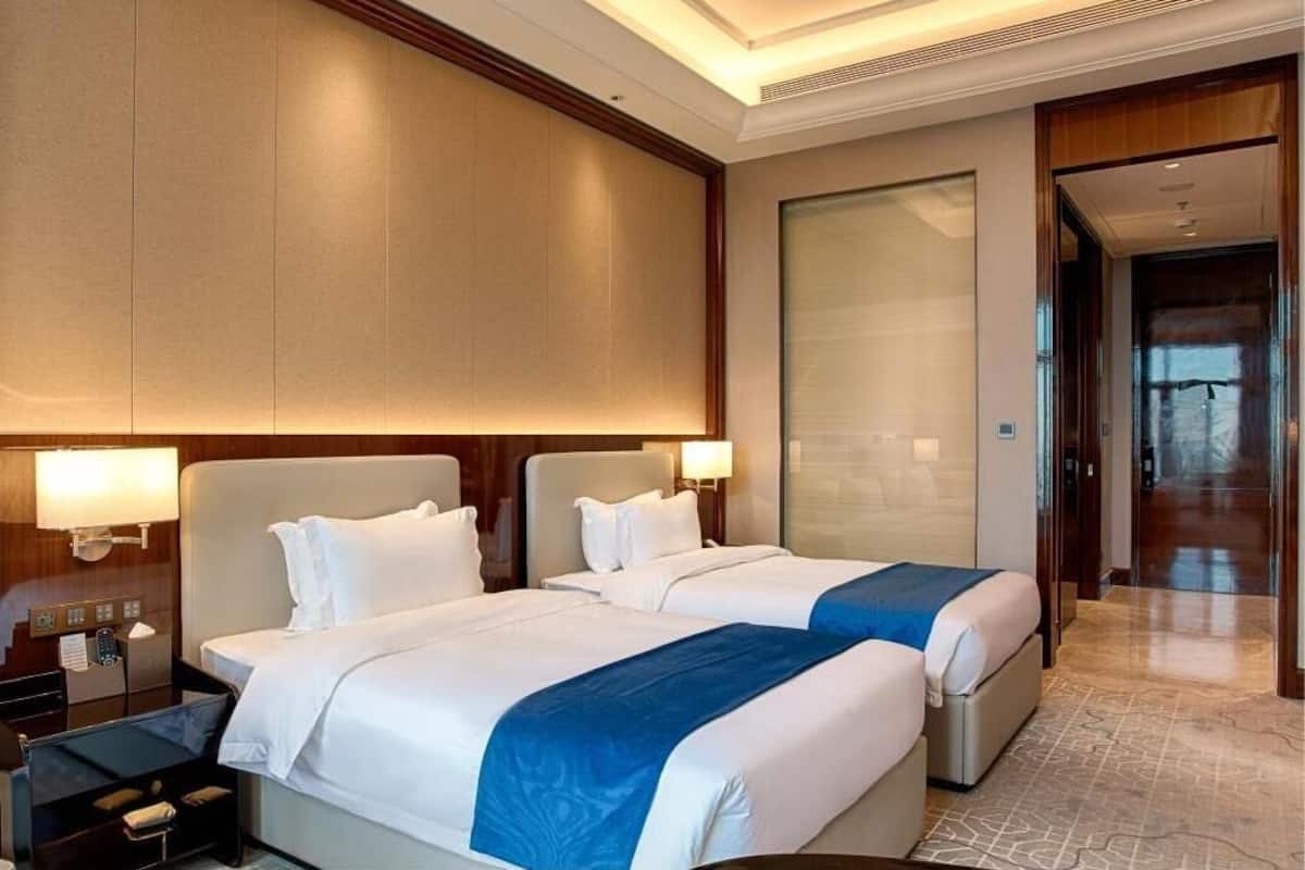 Quarto de hotel com duas camas, uma escrivaninha e uma mesa de cabeceira.