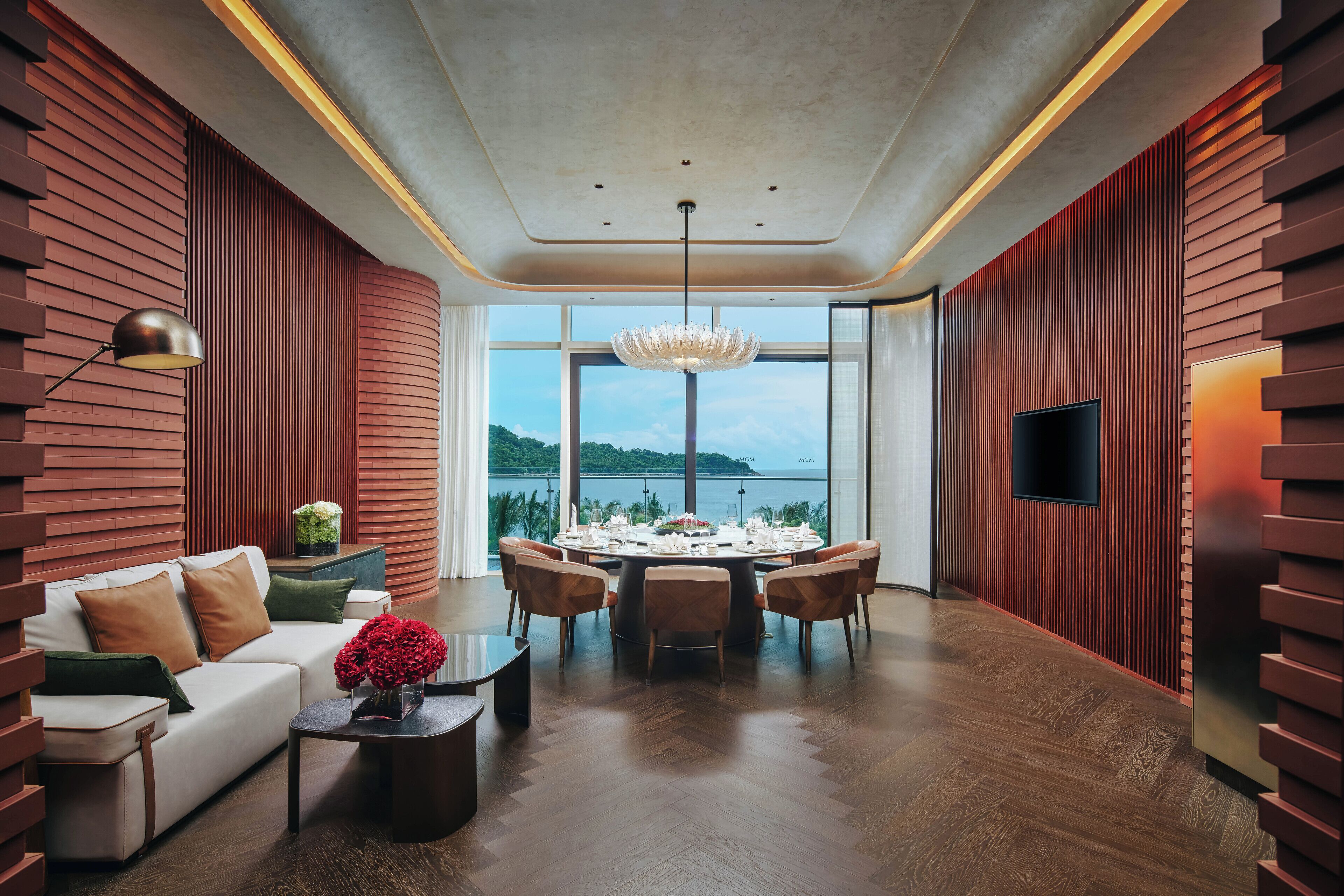 Uma área de jantar moderna com uma mesa redonda posta para seis pessoas, cercada por painéis de madeira e grandes janelas que oferecem uma vista panorâmica.