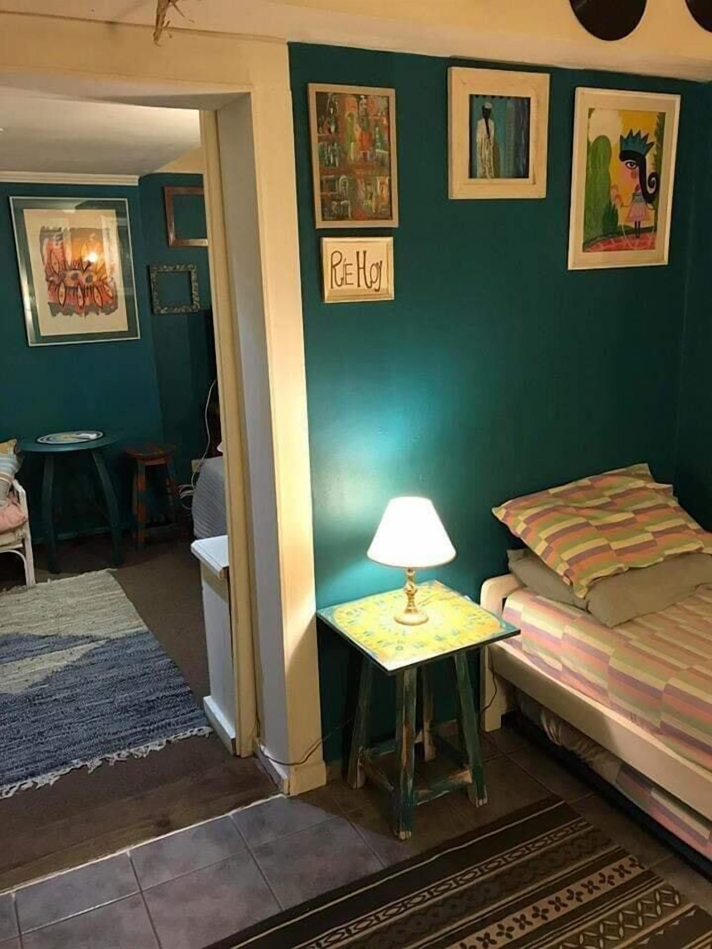 Quarto com paredes verde-água, cama com roupa de cama listrada, uma mesa pequena com abajur e várias obras de arte emolduradas.
