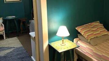 Quarto com paredes verde-água, cama com roupa de cama listrada, uma mesa pequena com abajur e várias obras de arte emolduradas.