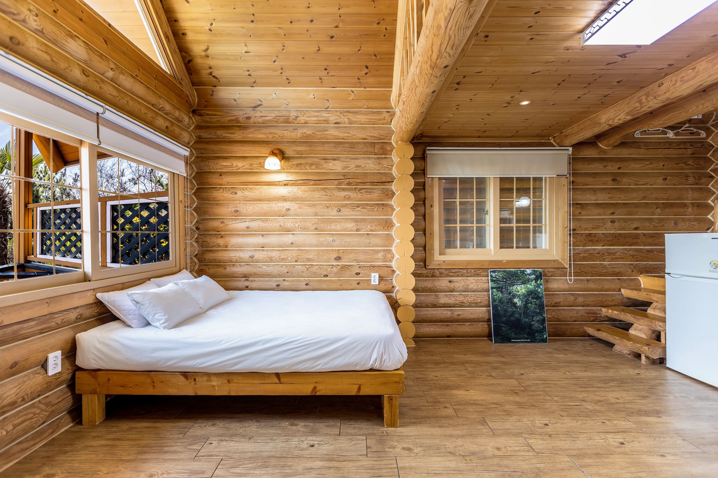 Interior de uma cabana de madeira com cama, janela com vista e pequena cozinha.