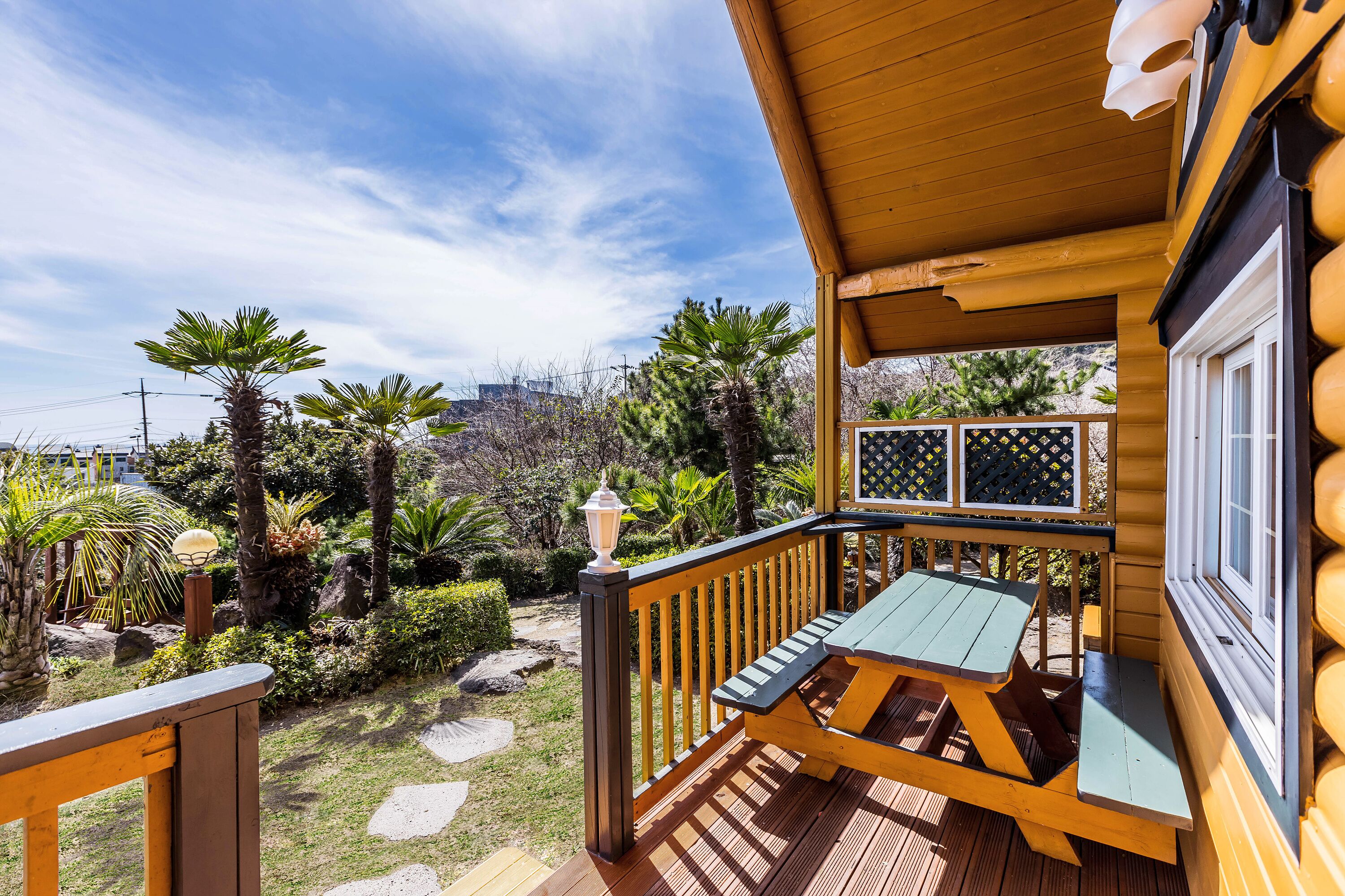 Um deck de madeira com mesa e bancos, cercado por vegetação exuberante e vista para a cidade.