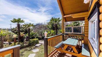 Um deck de madeira com mesa e bancos, cercado por vegetação exuberante e vista para a cidade.