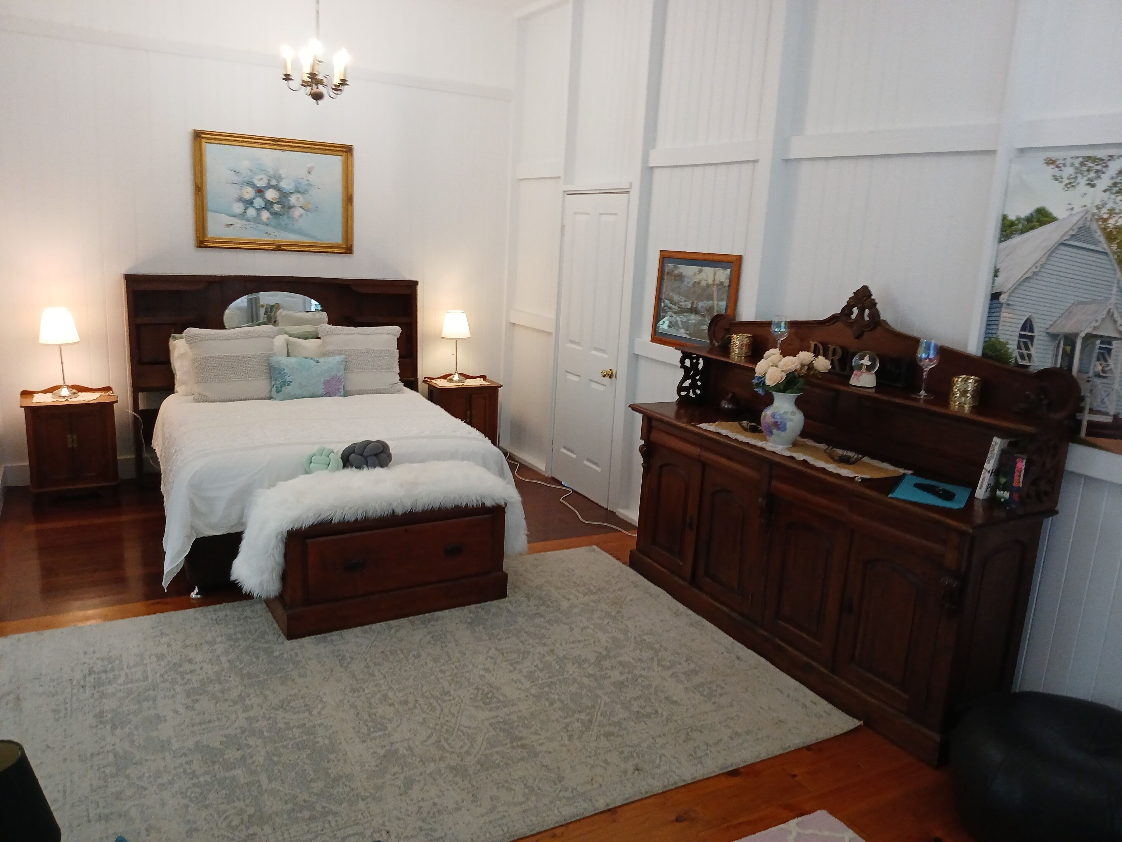 Quarto com uma cama grande, duas mesas de cabeceira com abajures, cômoda e um candelabro.