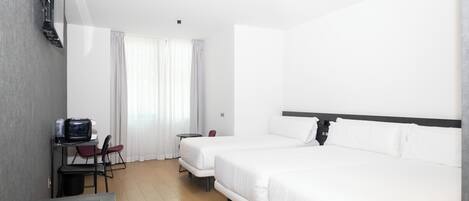 Quarto de hotel com duas camas de solteiro, uma escrivaninha com cadeira, uma mesinha e uma televisão fixada na parede.