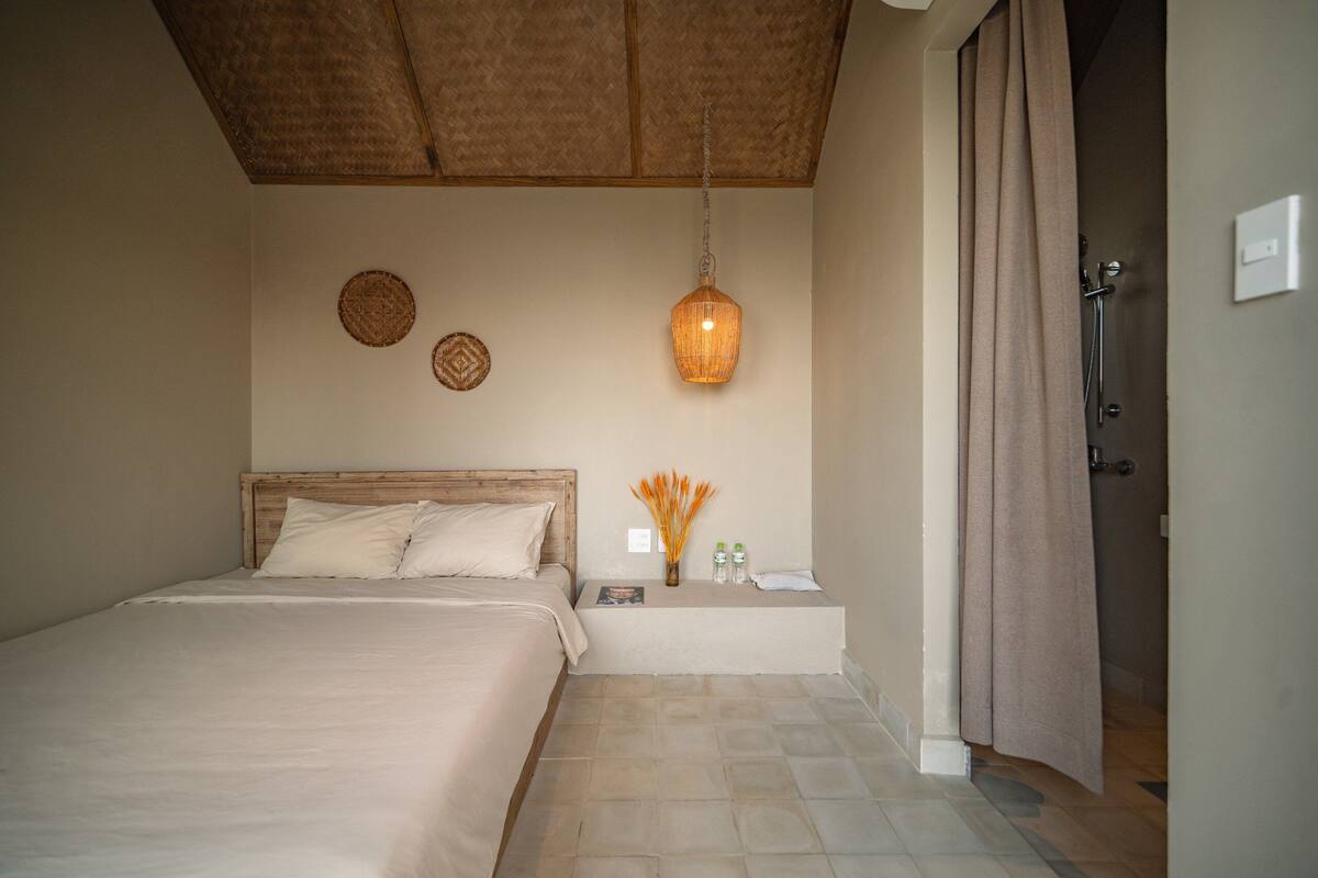 Quarto com cama, mesa de cabeceira e luminária suspensa.