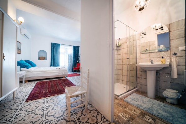 Quarto com cama, poltrona, tapete vermelho e banheiro com pia e chuveiro.