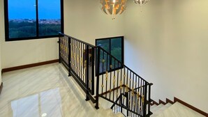 Um quarto amplo com uma grande janela, uma escada com corrimão preto e duas luminárias esféricas no teto.
