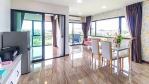 Quarto de hotel moderno com varanda, área de jantar com mesa e cadeiras, e uma TV em um móvel.