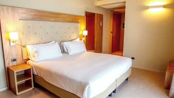 Quarto de hotel com uma cama grande, cabeceira de madeira, mesas de cabeceira e luzes fixadas na parede.