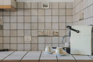 Uma cozinha com máquina Nespresso, duas chávenas com pires e um painel de azulejos.
