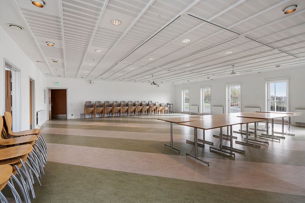 Uma sala de conferências espaçosa com teto alto, várias mesas e cadeiras dispostas para reuniões.