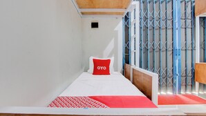 Uma cama de solteiro com travesseiro vermelho, roupa de cama branca e um edredom com padrão vermelho e branco.