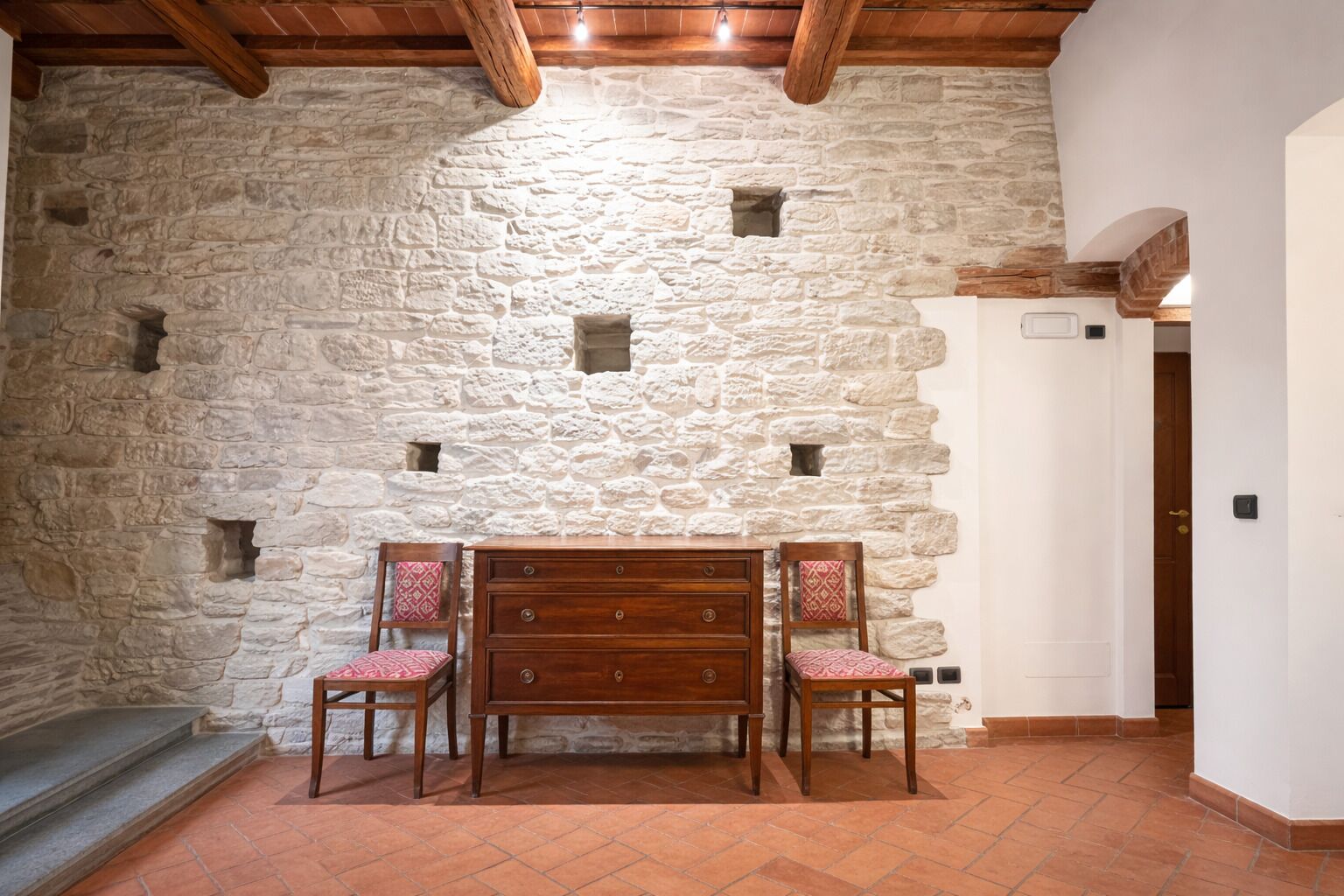 Um quarto com parede de pedra, móveis de madeira e piso de azulejos.
