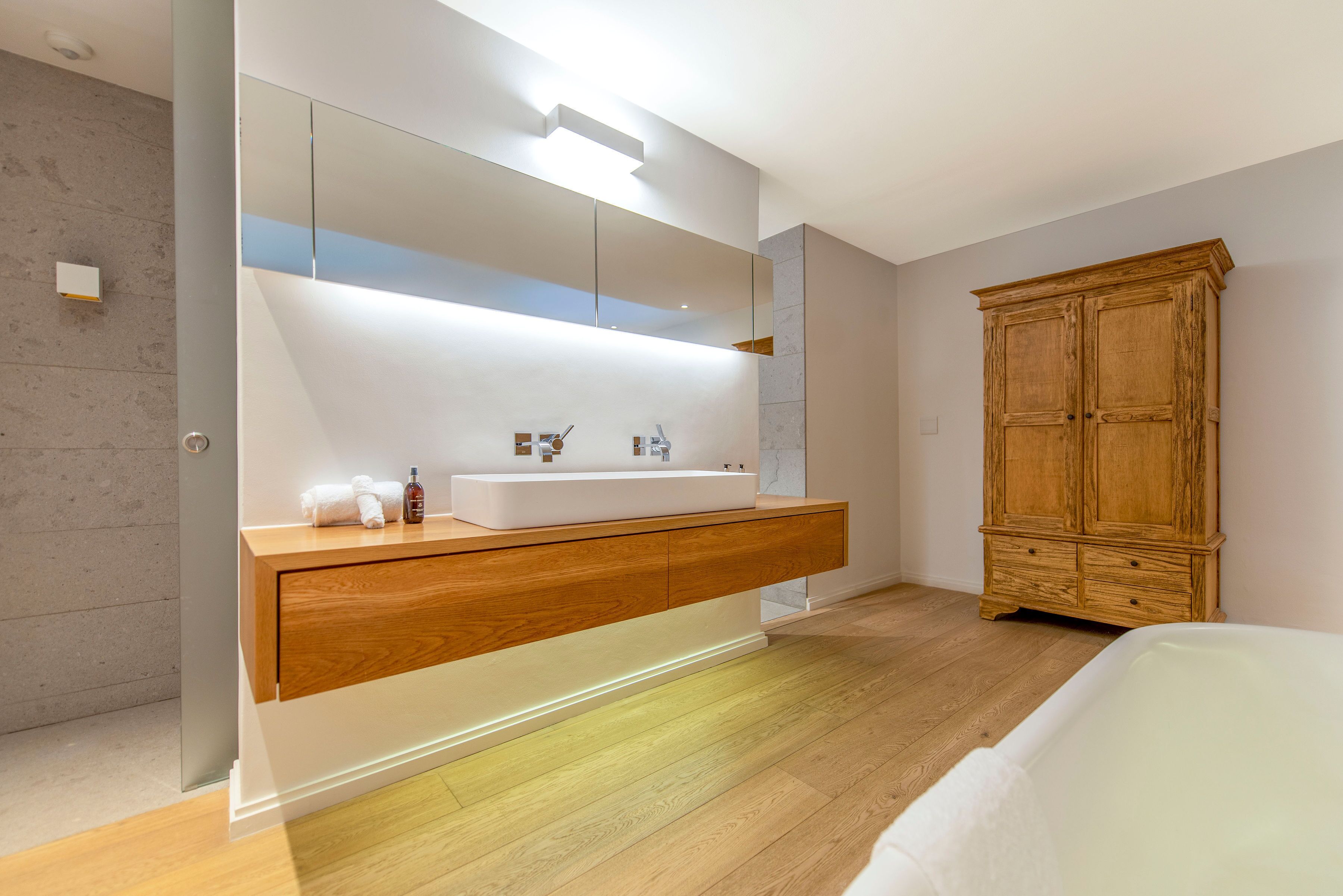 Uma casa de banho moderna com um espelho grande, toucador de madeira e guarda-roupa de madeira.
