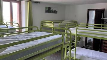 Um dormitório com beliches, uma janela com cortinas, uma mesa pequena com abajur e um quadro na parede.