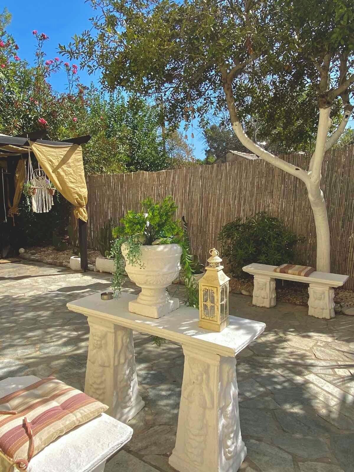 Um pátio externo com mesas de pedra, um banco e um candeeiro decorativo.