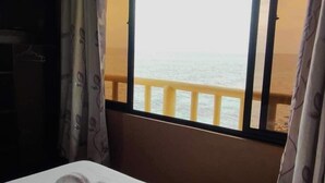 Um quarto com cama, janela e vista para o mar, e cortinas.