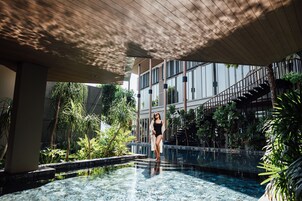 Uma mulher de fato de banho preto está na beira de uma piscina com teto de madeira e uma escadaria ao fundo.