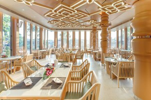 Uma sala de jantar espaçosa com várias mesas e cadeiras, amplas janelas com vista para o exterior e um design de teto moderno.