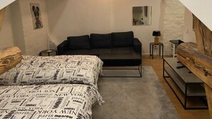 Um quarto de sótão acolhedor, com um sofá escuro, uma cama com roupa de cama estampada, uma mesinha e um espelho na parede.