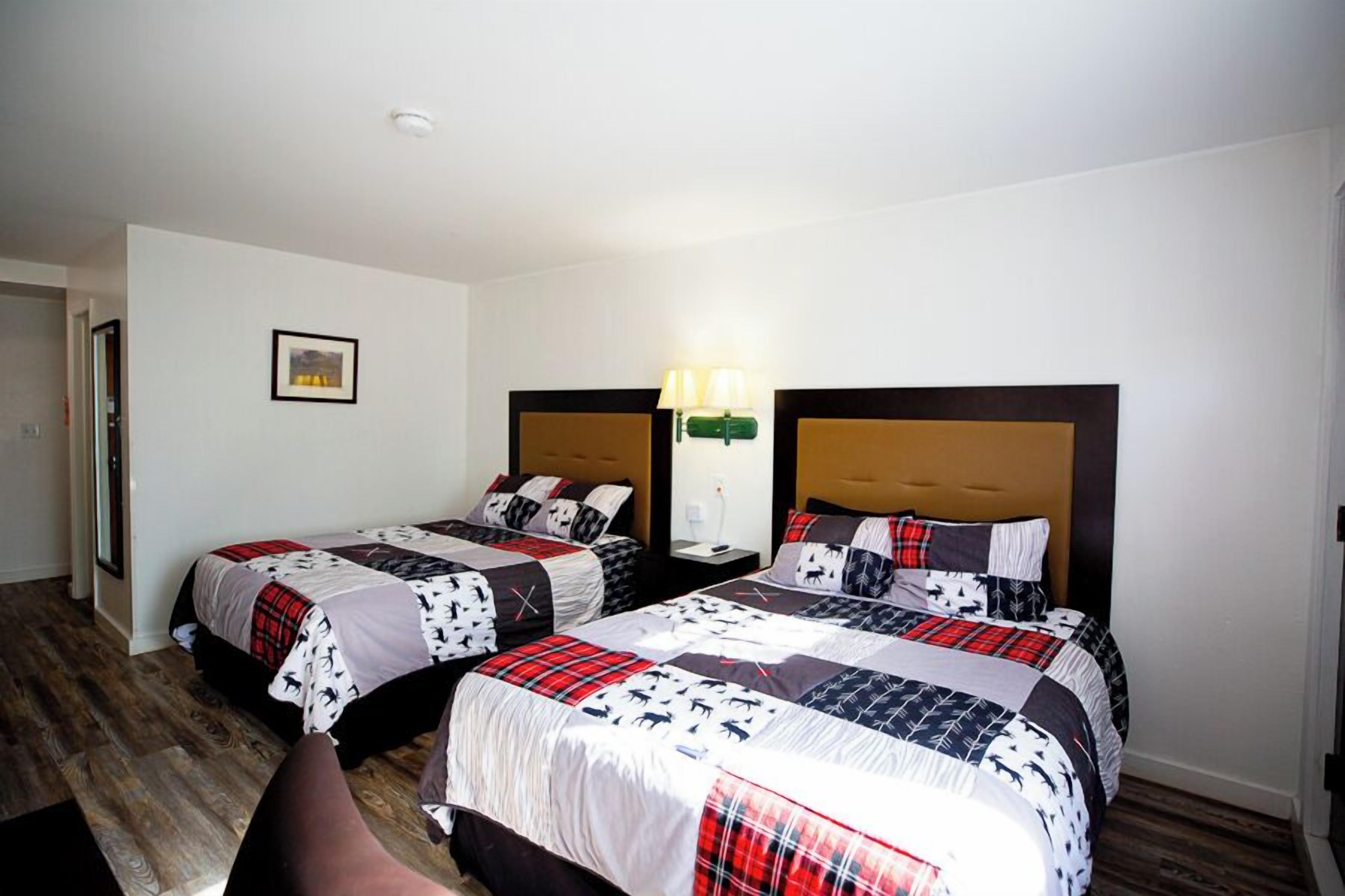 Quarto de hotel com duas camas, cada uma com cabeceira, mesa de cabeceira e luminária.